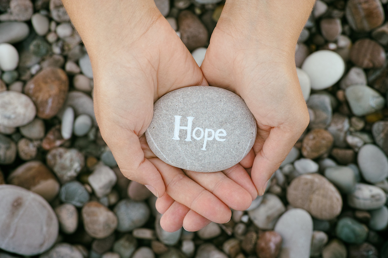 Woman holding stone with the word Hope in her palms - Eglise Pleine Vie